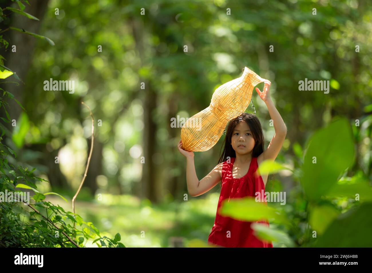 Little asian girl in red dress holding fishing equipment in the forest, Rural Thailand living ...
