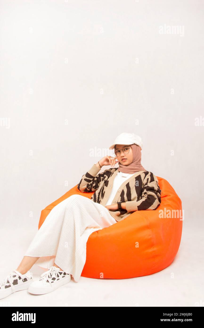 portrait of beautiful young woman in glasses and hat sitting on orange ...