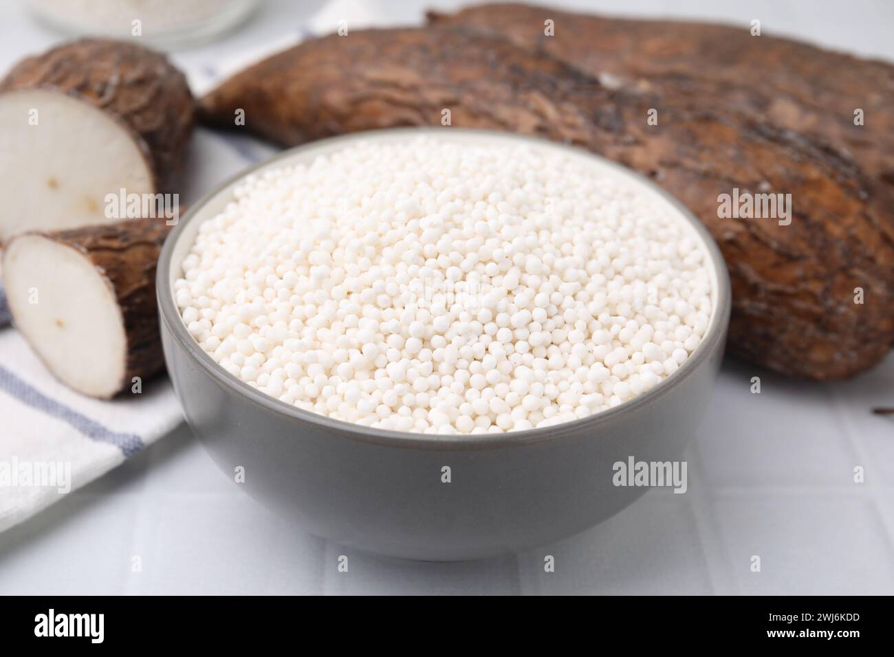 Tapioca pearls in bowl and cassava roots on white tiled table, closeup ...