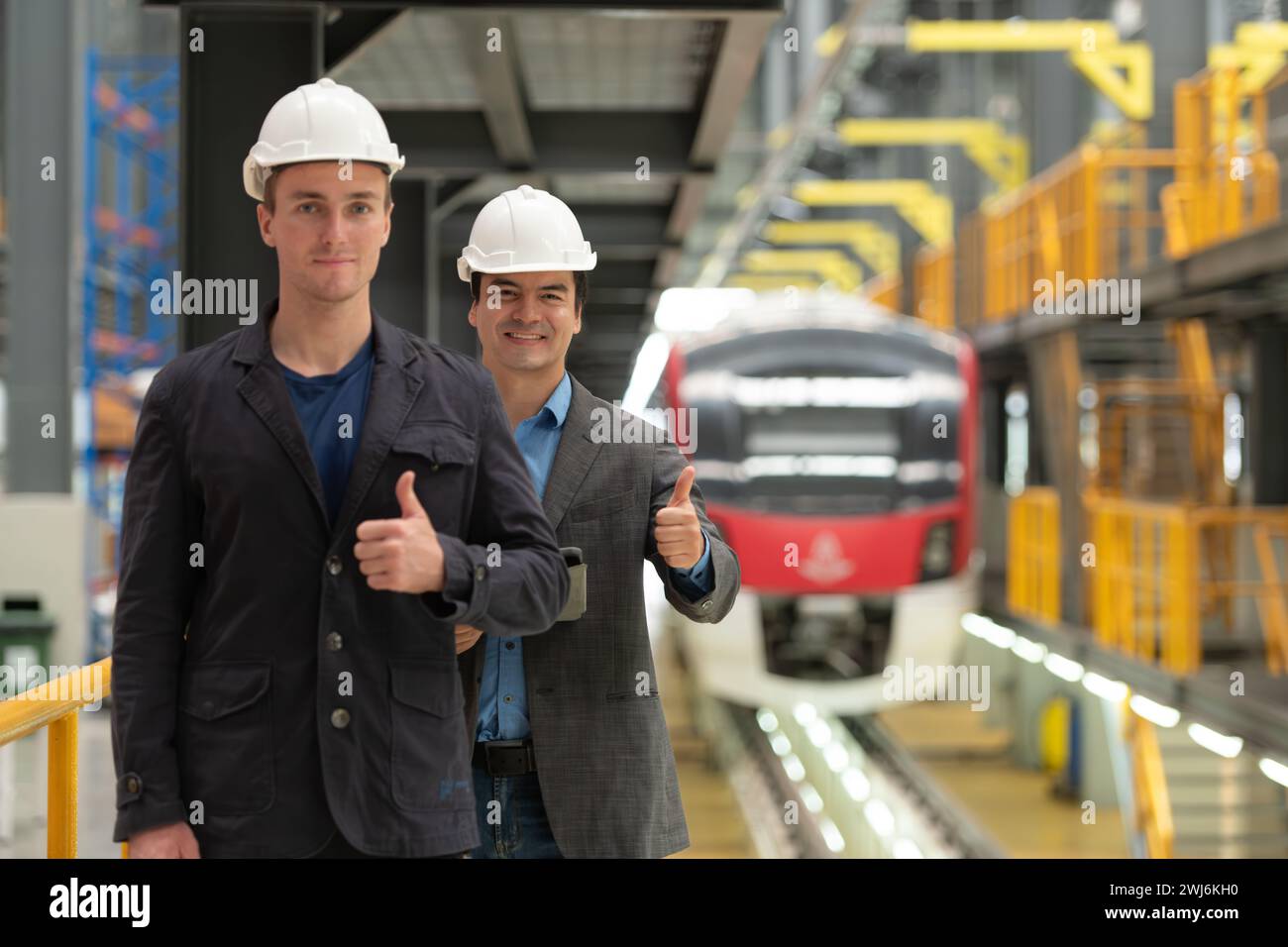 Portrait of two young engineers showing thumbs up in front of train station Stock Photo - Alamy