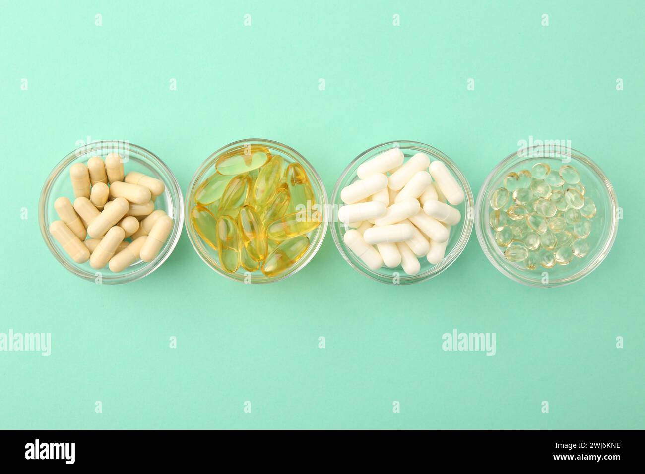 Different vitamin capsules in glass bowls on turquoise background, flat ...