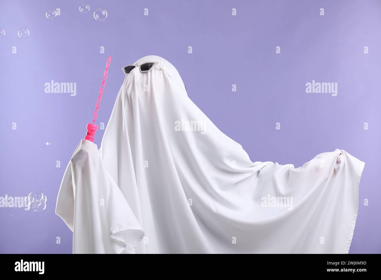 Funny ghost. Person in white sheet and sunglasses blowing soap bubbles ...