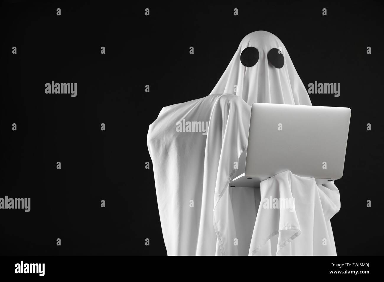 Creepy ghost. Person in white sheet with laptop on black background ...
