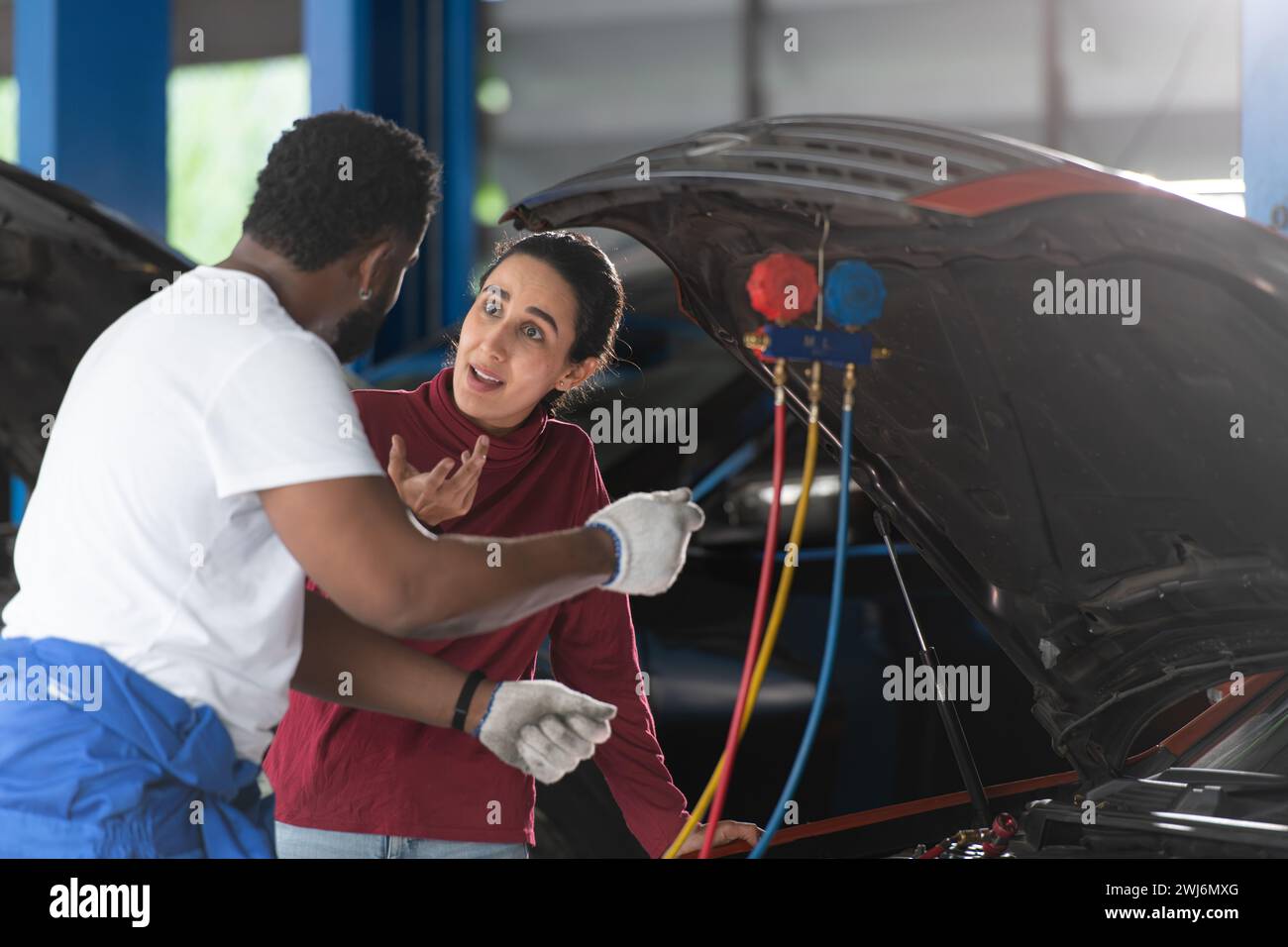 Car mechanic working in an auto repair shop explain to customer after inspecting the operation ...