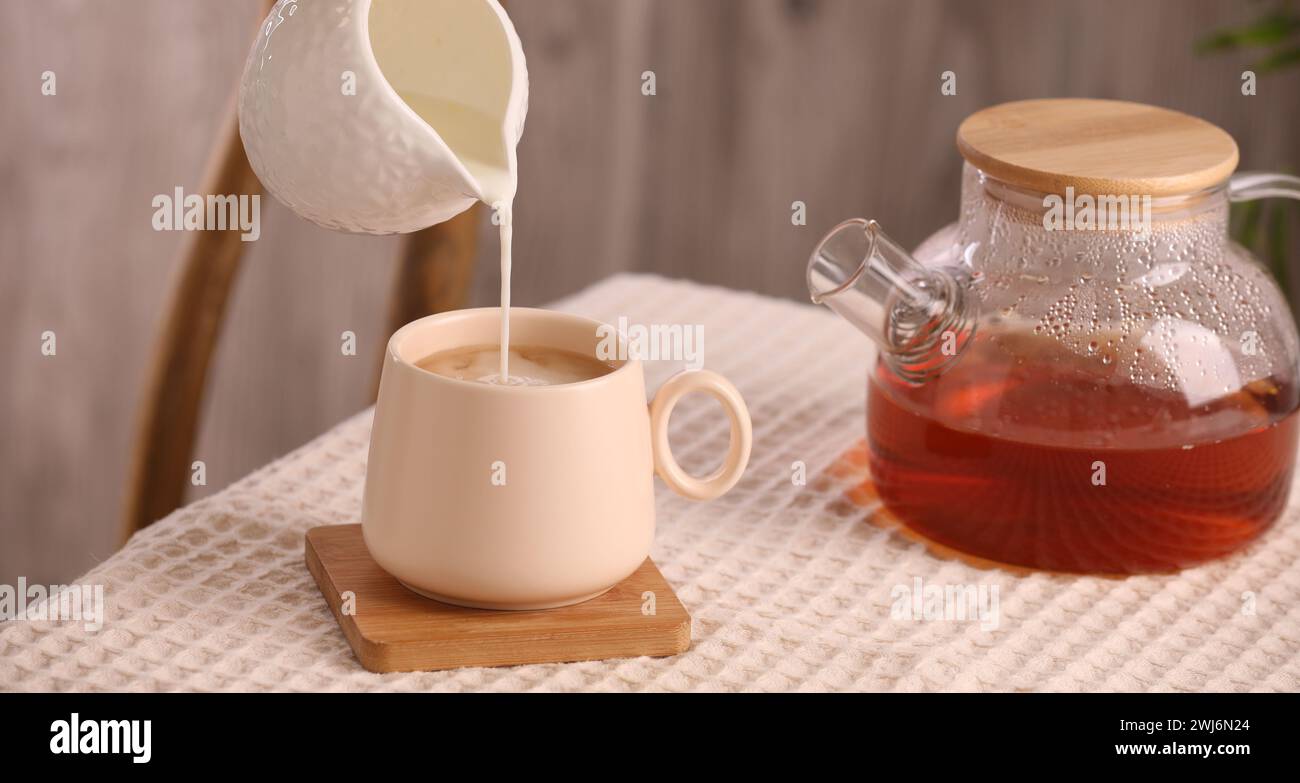Pouring milk into cup with aromatic tea at table Stock Photo - Alamy