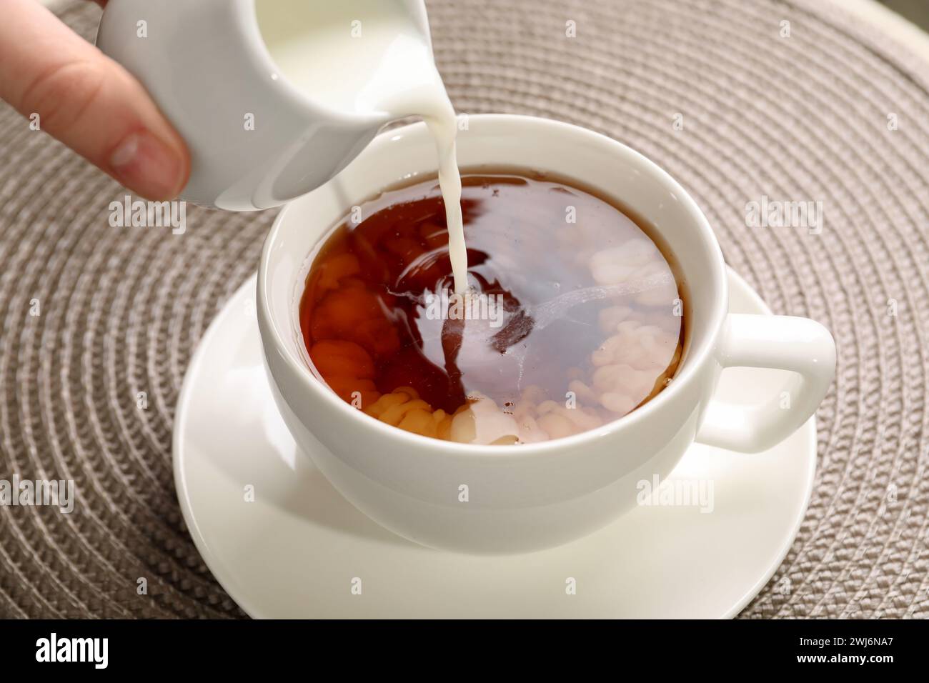 Woman pouring milk into cup with aromatic tea at table, closeup Stock ...