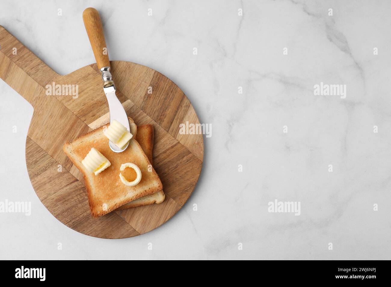 Tasty butter curls, knife and toasts on white marble table, top view ...