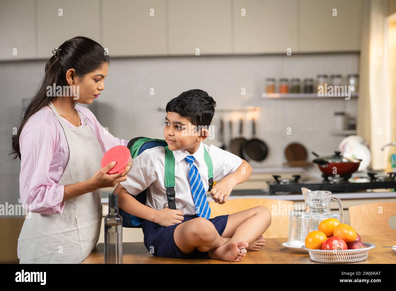 Caring Indian mother preparing kid for school by placing lunch box and ...