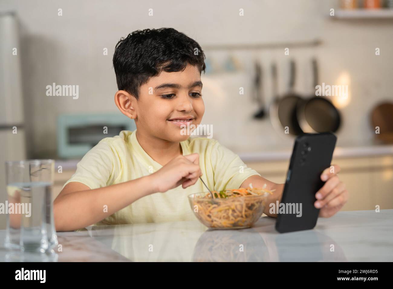Indian preteen kid eating noodles while using mobile phone at home on ...