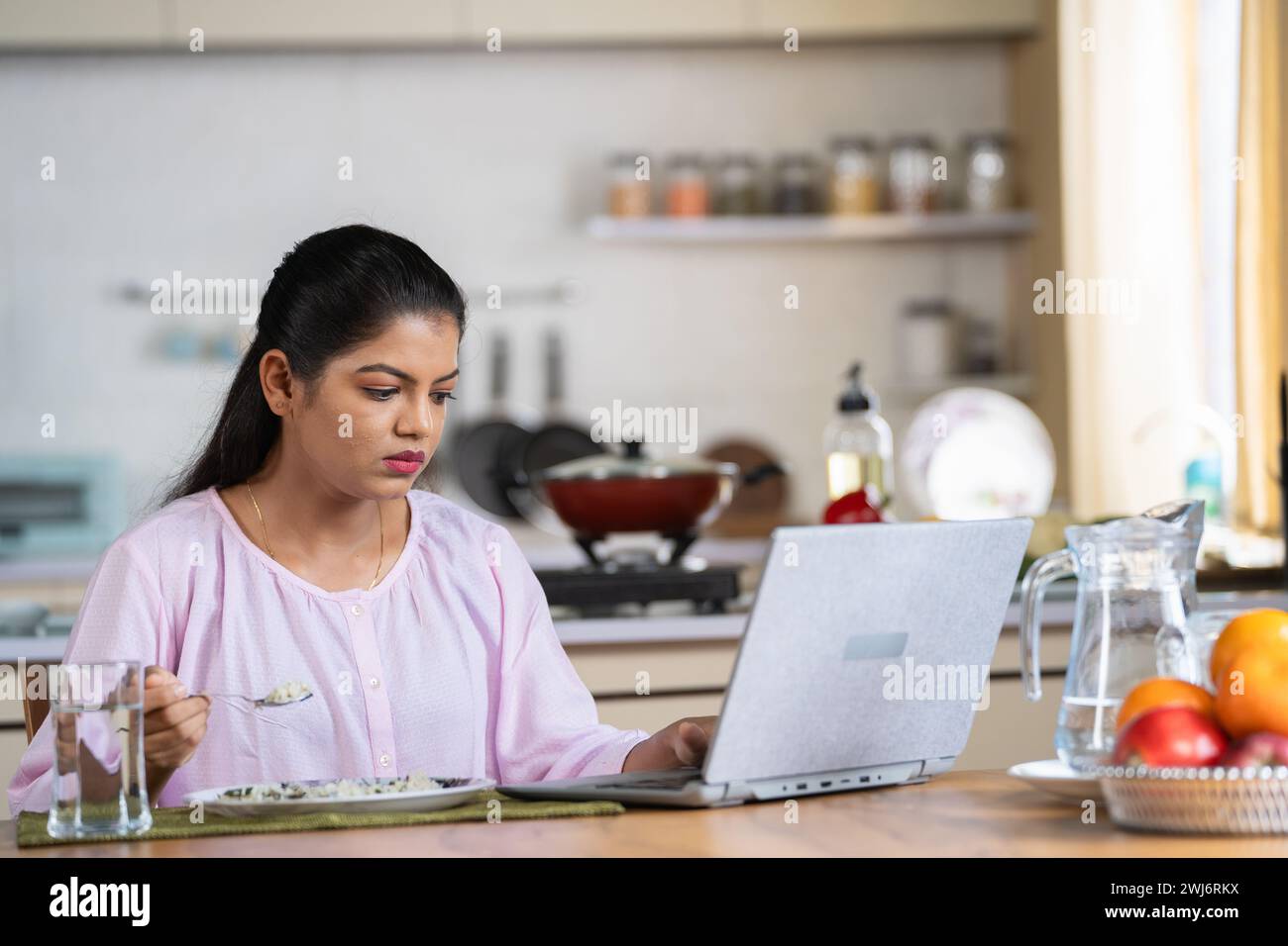 Indian businesswoman working on laptop while eating at dining table ...