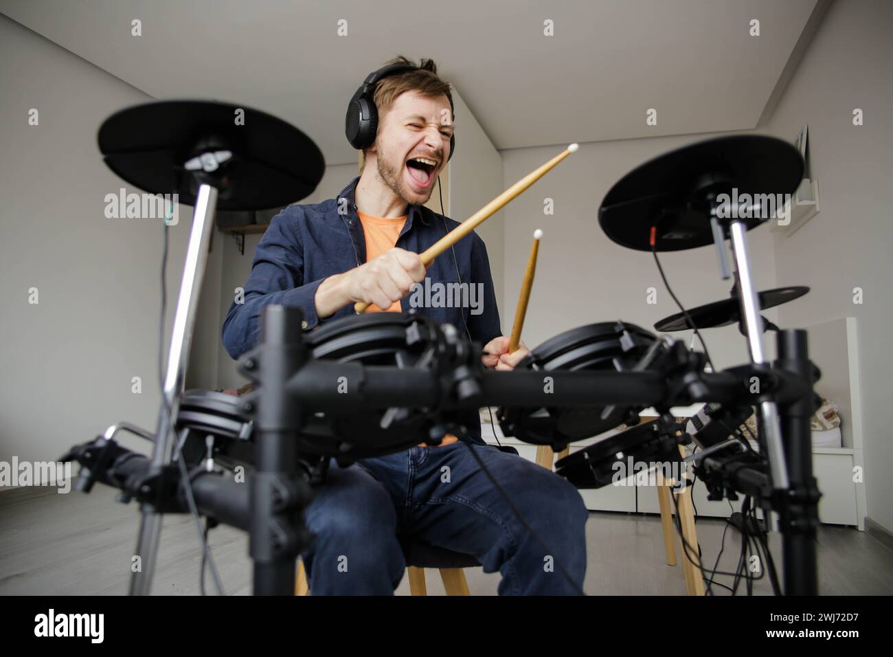Excited young man with headphones hitting electric drum set during ...