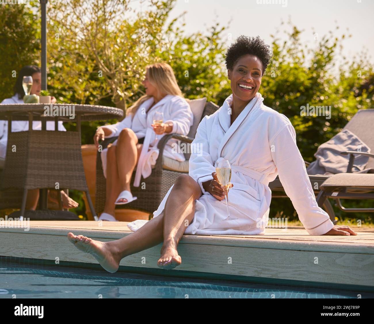 Mature Woman Wearing Robe Sitting With Feet In Pool Drinking Champagne ...