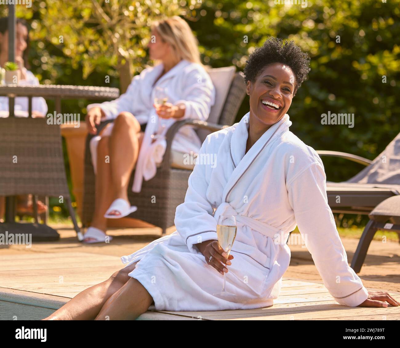 Mature Woman Wearing Robe Sitting With Feet In Pool Drinking Champagne ...