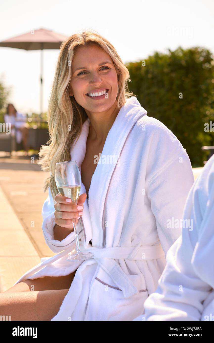 Mature Woman Wearing Robe Sitting By Pool Drinking Champagne On Spa Day ...