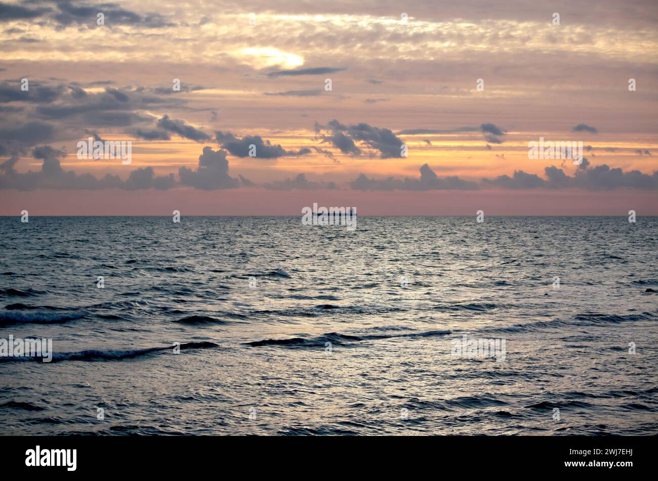 Serene sunset over choppy sea, silhouetted ships on horizon, sky ...