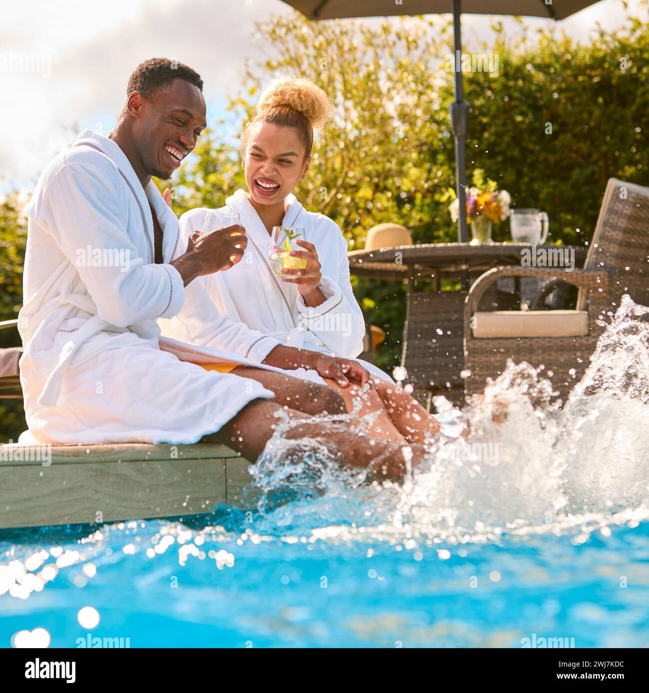 Loving Couple Wearing Robes Outdoors Sitting With Drinks Splashing Feet ...