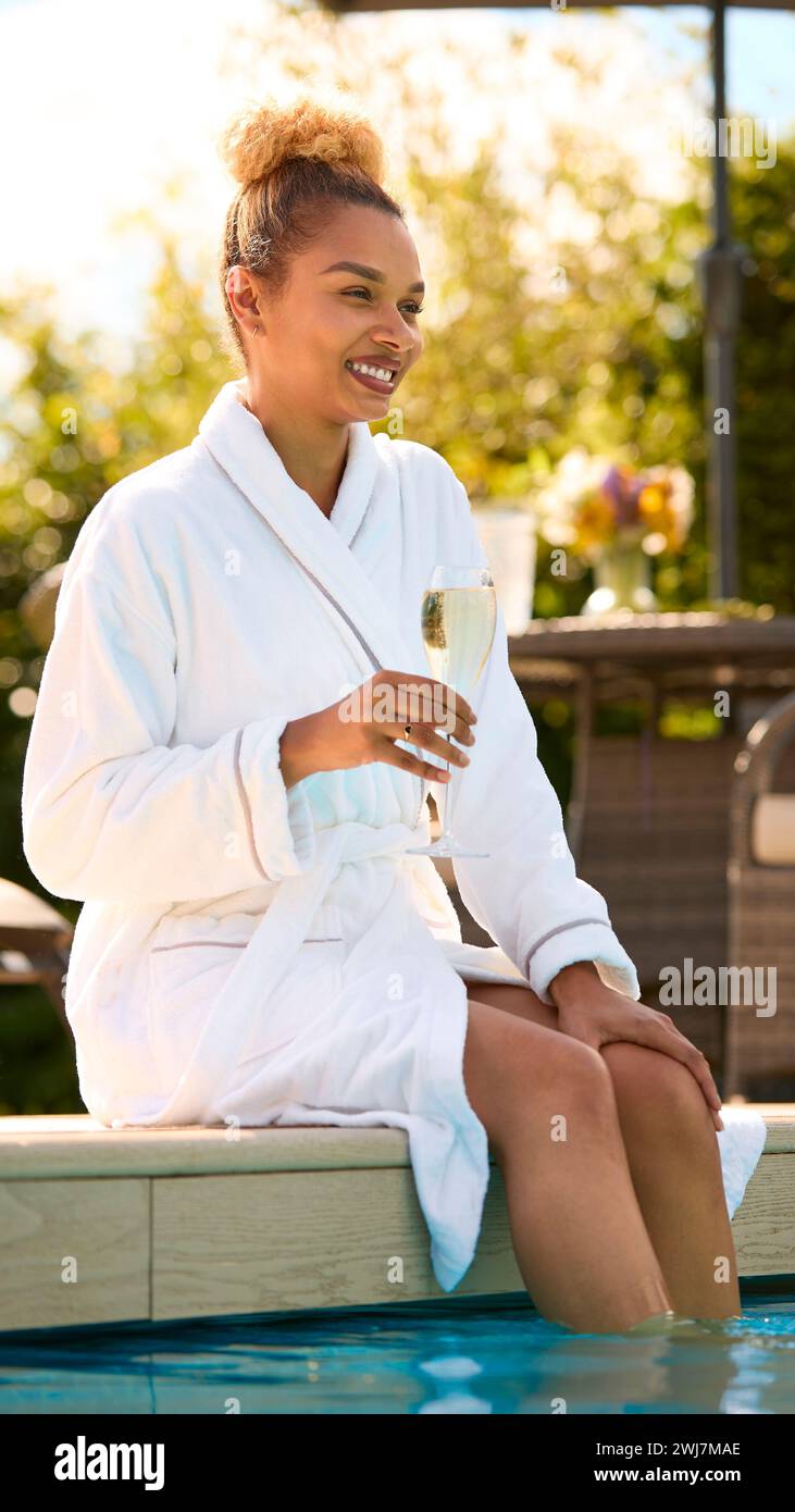 Woman In Robe Sitting Outdoors With Feet In Swimming Pool Drinking ...