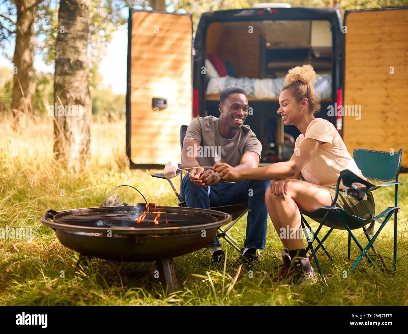 Couple Camping In Countryside With RV Toasting Marshmallows Outdoors On ...