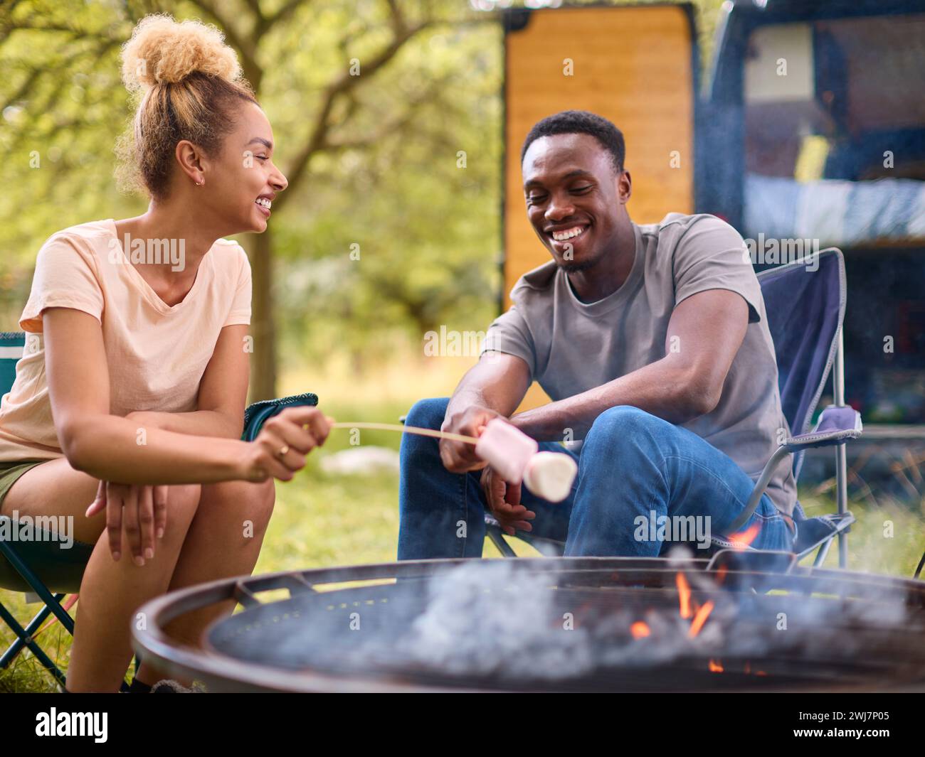 Couple Camping In Countryside With RV Toasting Marshmallows Outdoors On ...