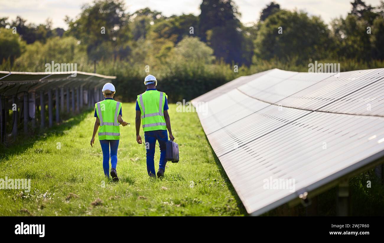 Rear View Of Male And Female Engineers Inspecting Solar Panels In Field ...