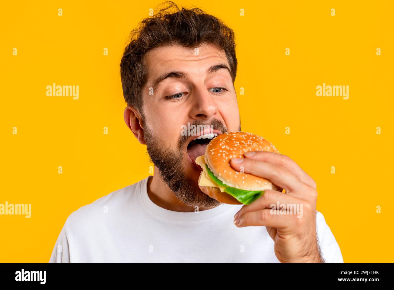 Man enjoying cheeseburger on cheat day on vibrant yellow backdrop Stock ...