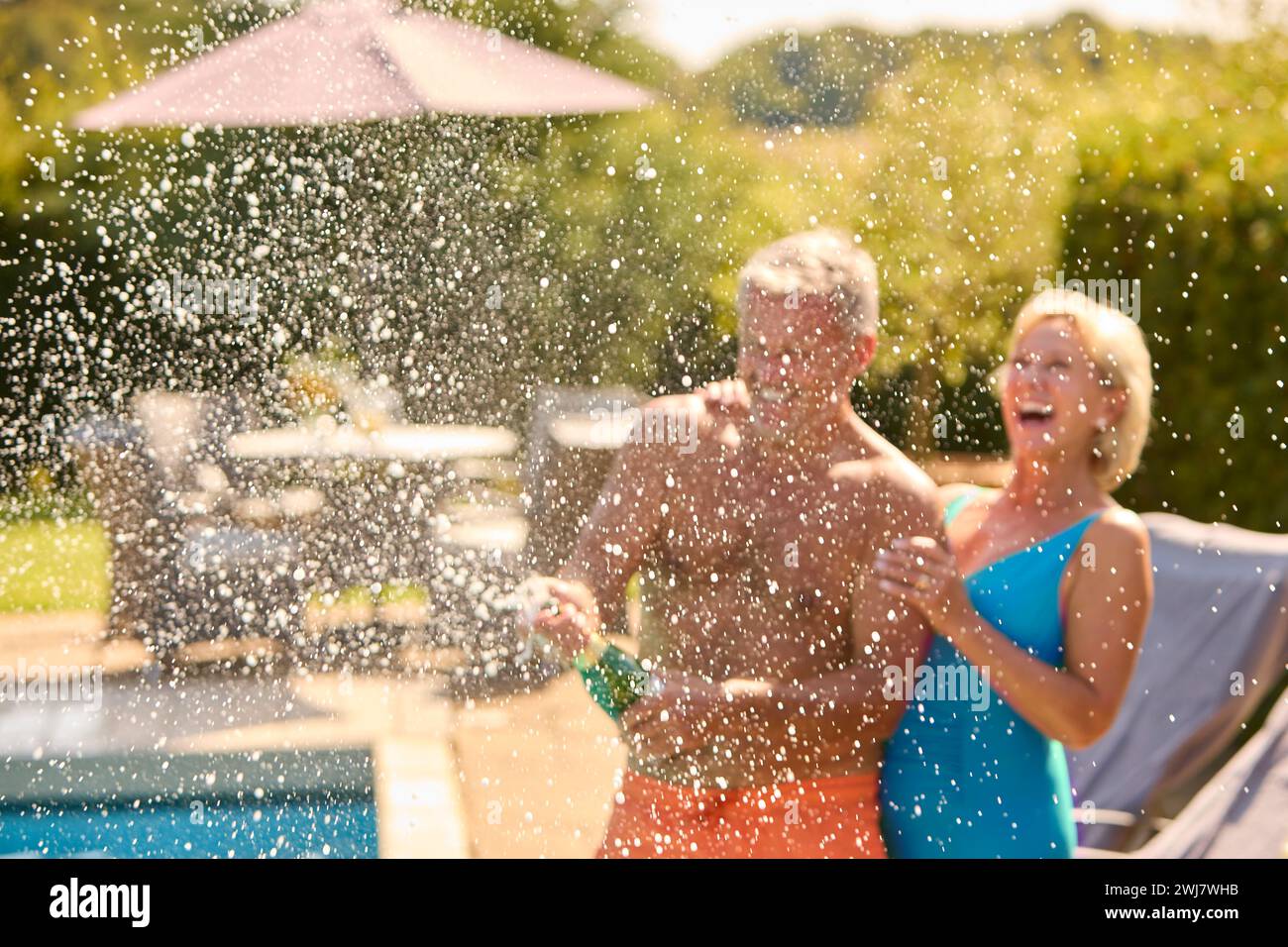 Senior Couple On Holiday In Swimming Costumes Opening Champagne By ...