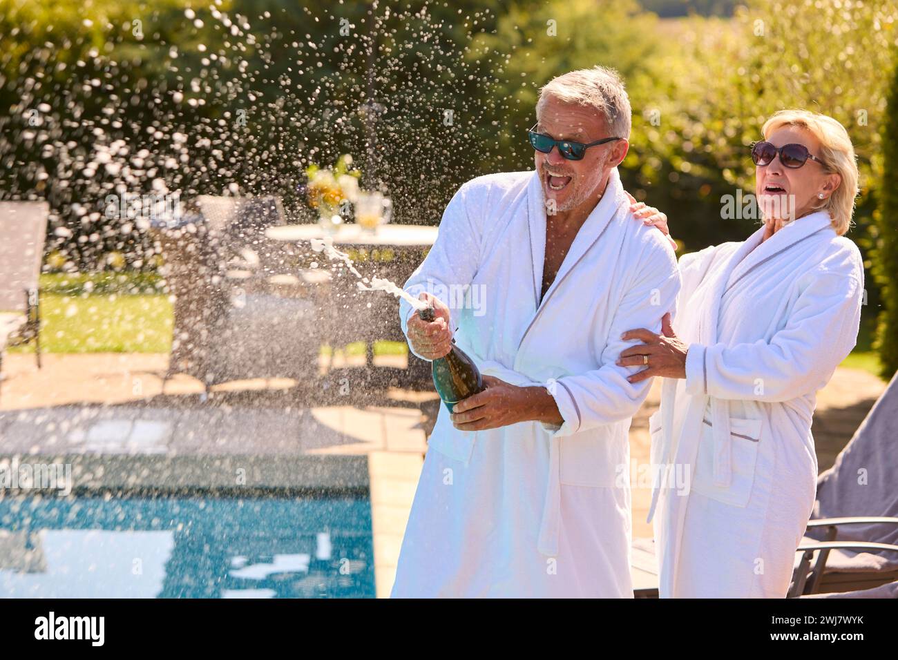 Senior Couple On Holiday Wearing Robes Opening Champagne By Hotel ...