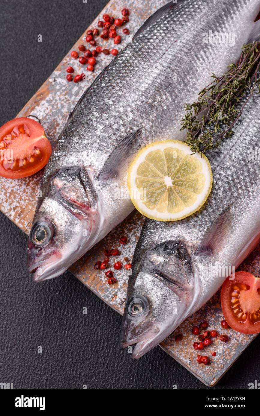 Fresh raw ocean sea bass fish with salt, spices and herbs on dark ...