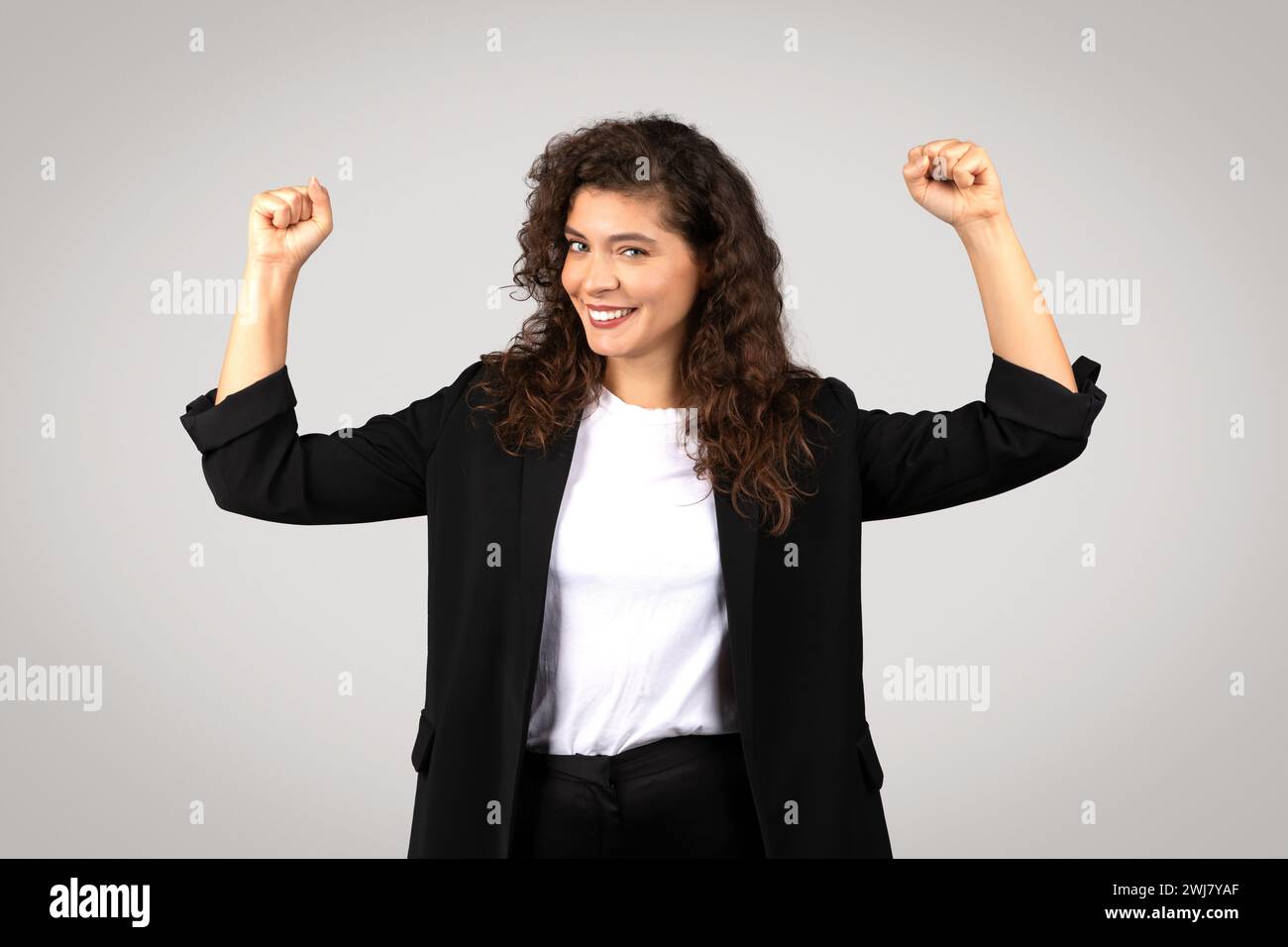 Exuberant young businesswoman with bright smile, raising her fists in ...