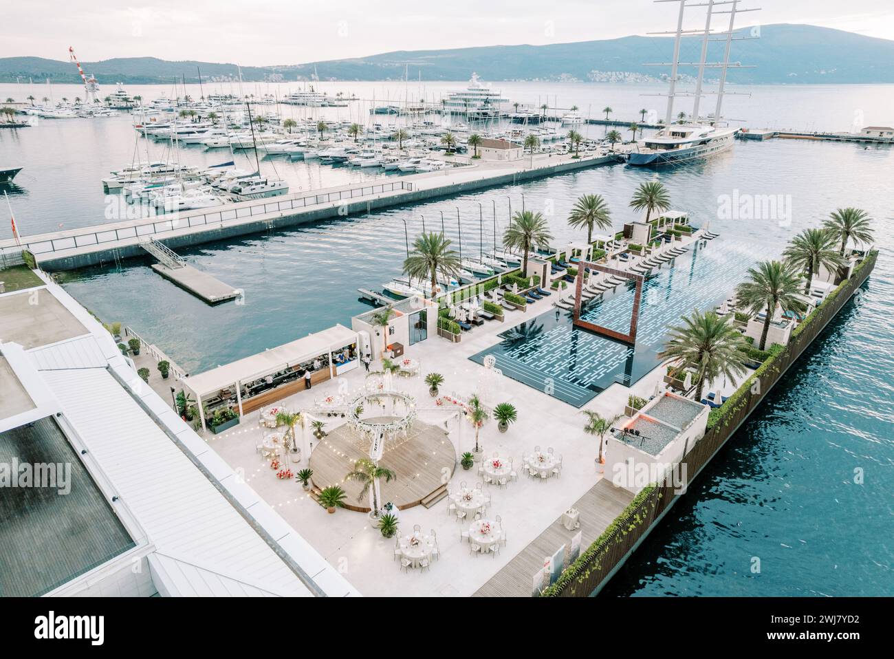 Round festive tables stand around a stage by the long pool on the pier ...
