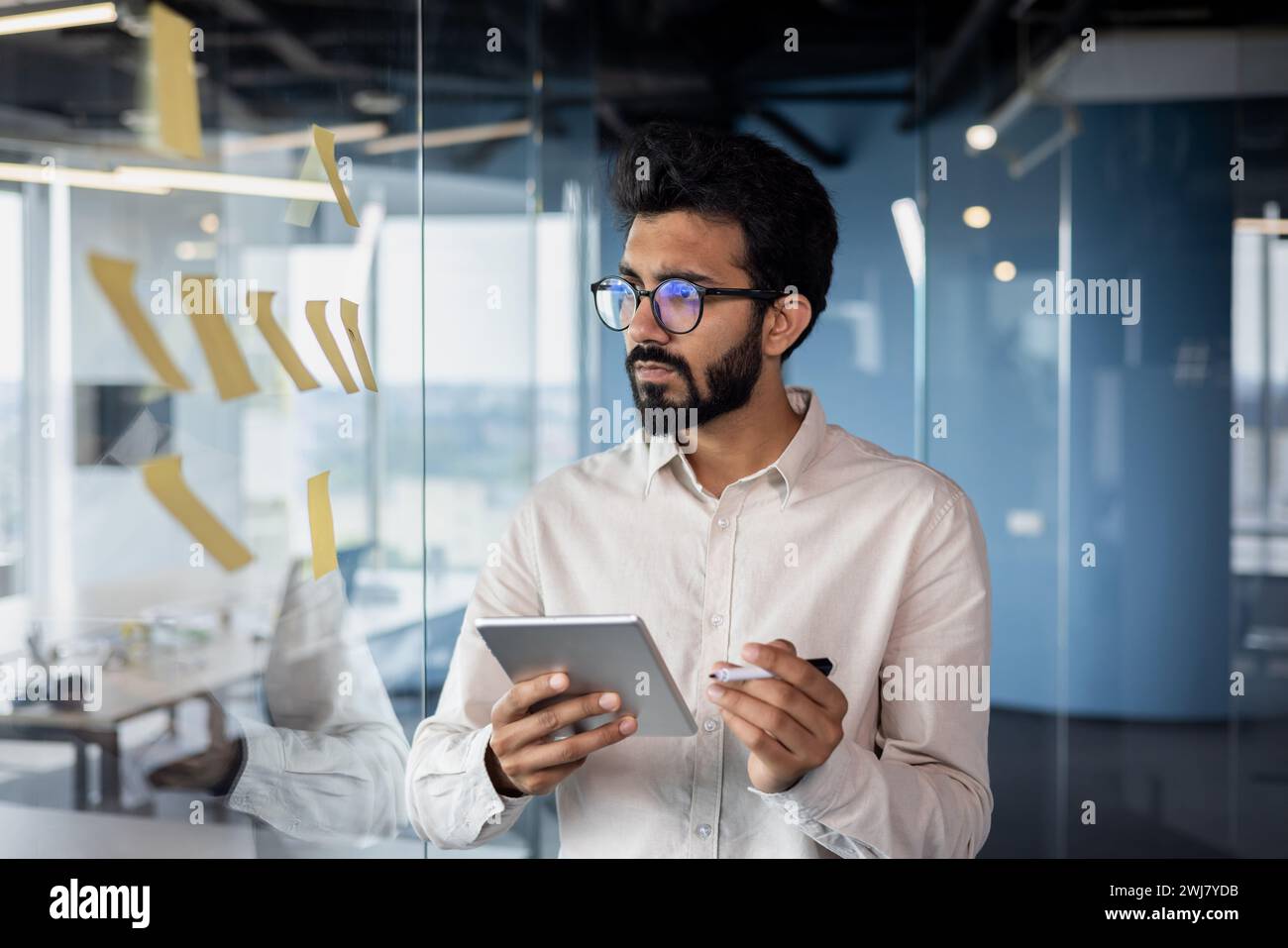 Serious and focused young Indian man working in office with tablet ...