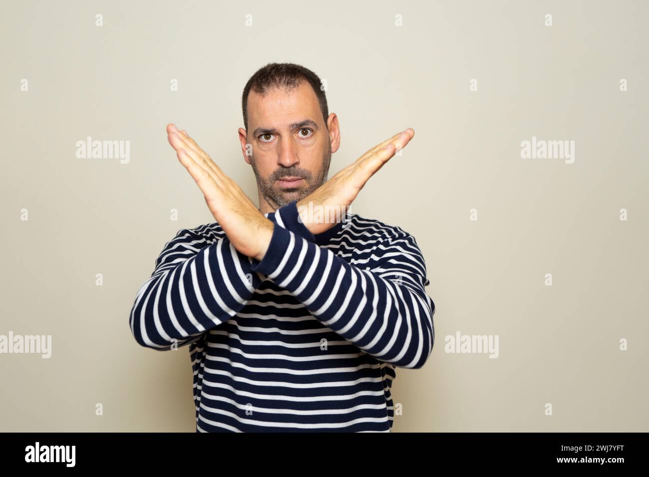 Portrait of serious Hispanic man with hands crossed, showing x sign ...