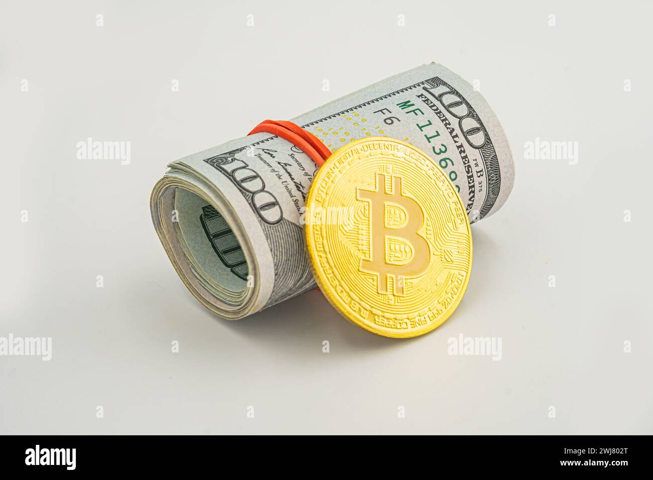 bitcoin BTC coin and roll of dollar bills banknotes white background ...