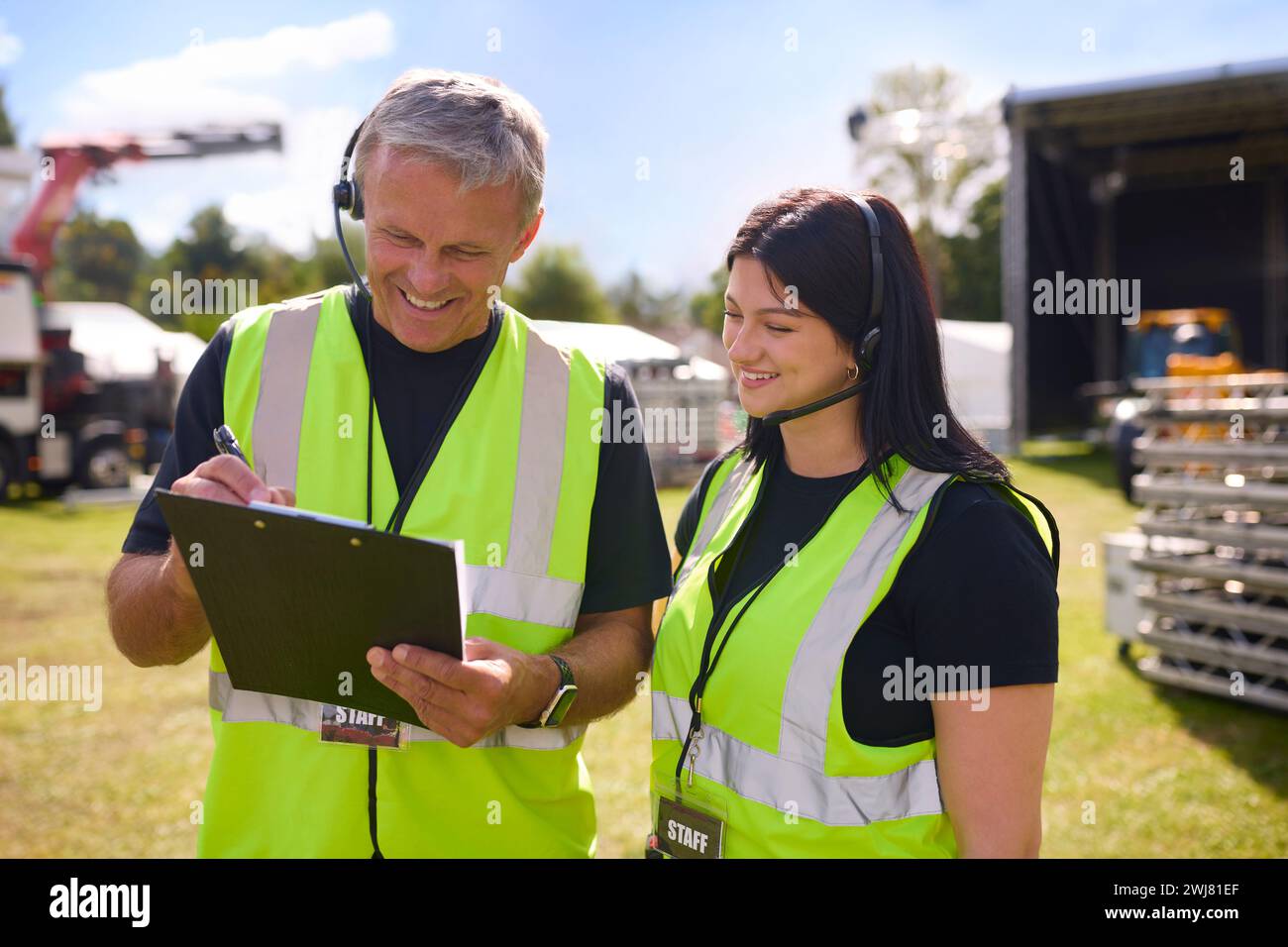 Male And Female Production Team With Headsets Setting Up Outdoor Stage ...