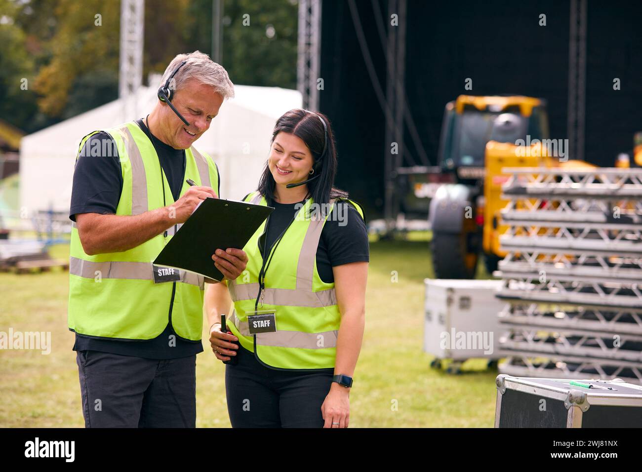 Male And Female Production Team With Headsets Setting Up Outdoor Stage ...