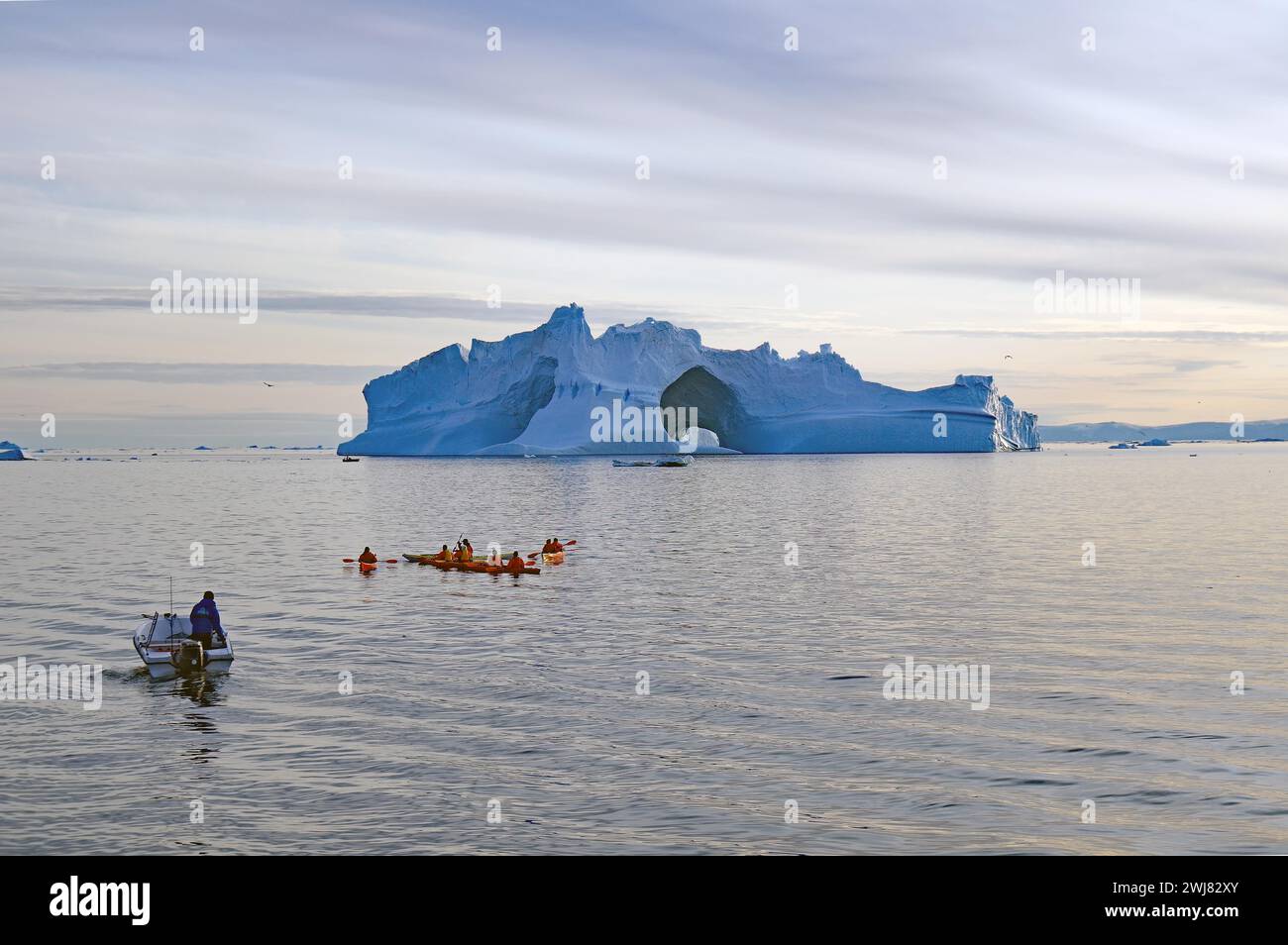 Small boat and kayaker in front of iceberg with large ice cave ...