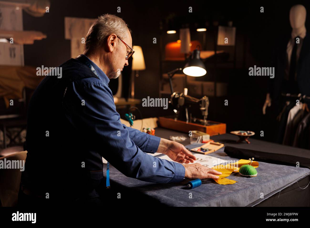 Professional elderly tailor working with sewing materials to customize ...
