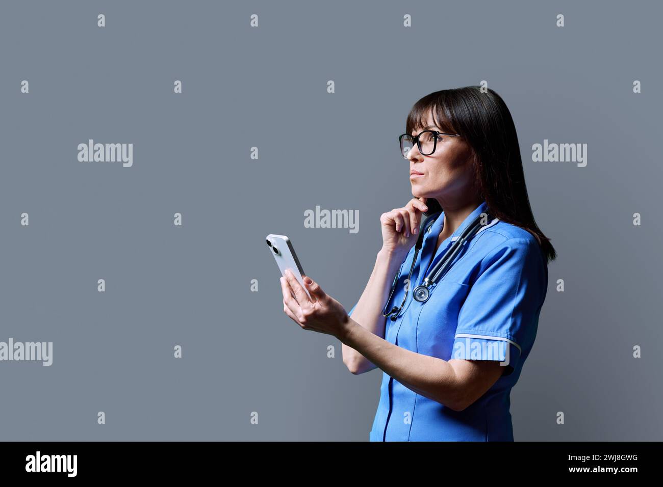 Female nurse using smartphone, profile view on gray studio background ...