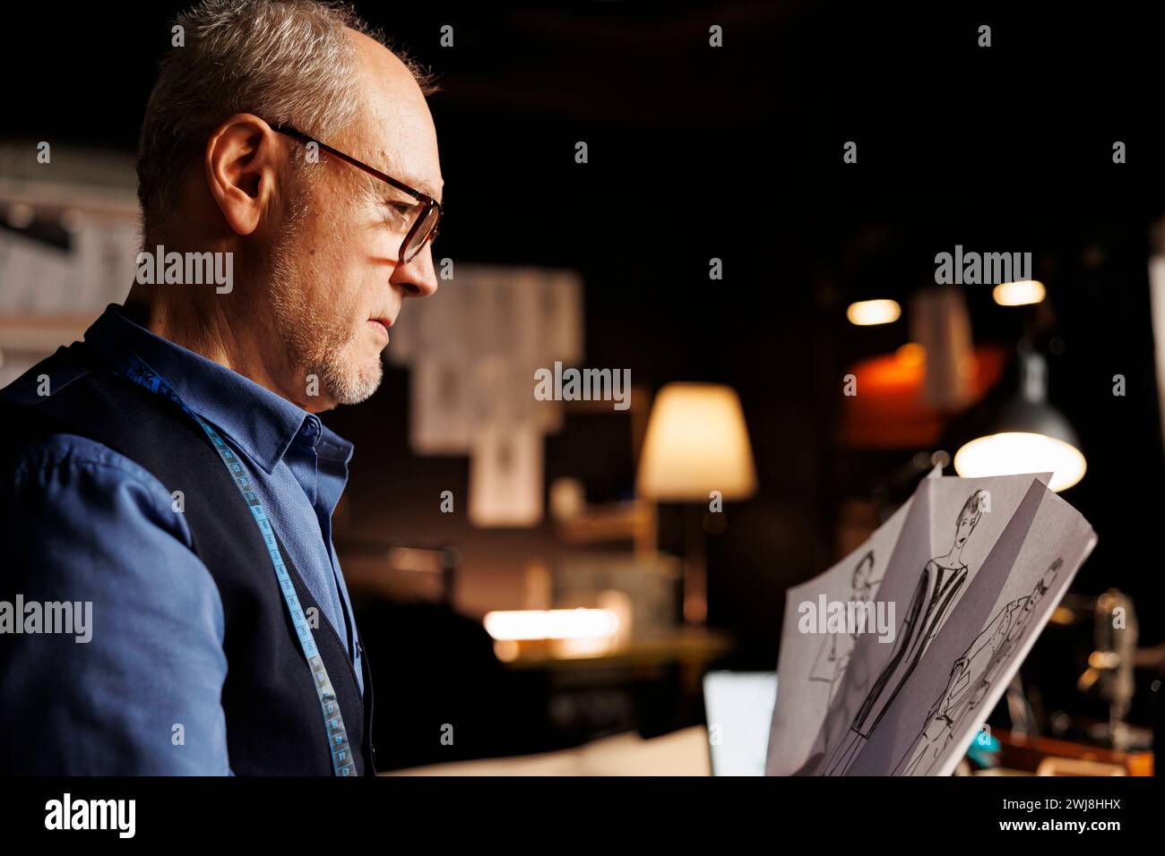 Close up of elderly suitmaker comparing handdrawn sketch designs ...