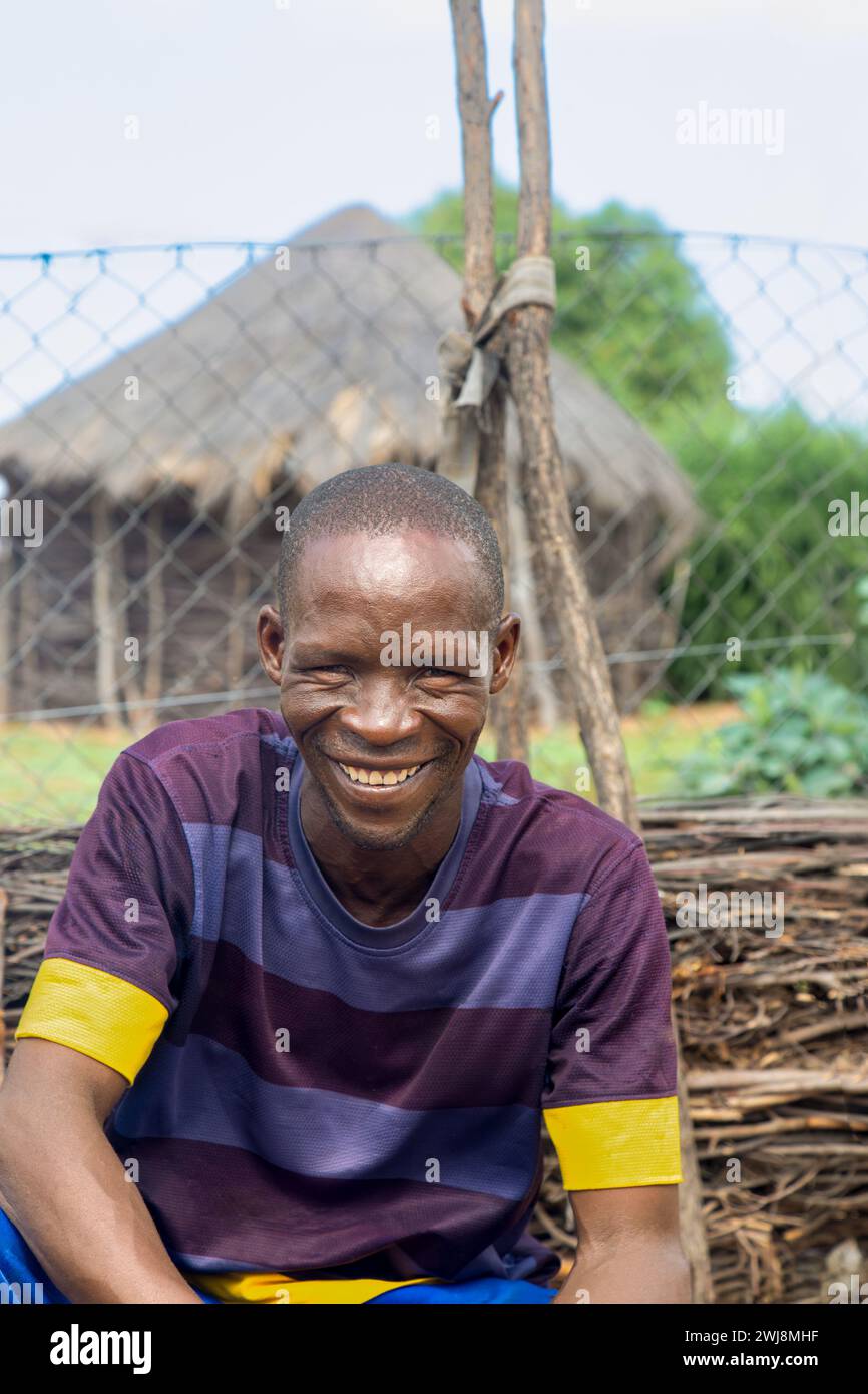 african man in the village, standing in the yard , mud houses shacks ...