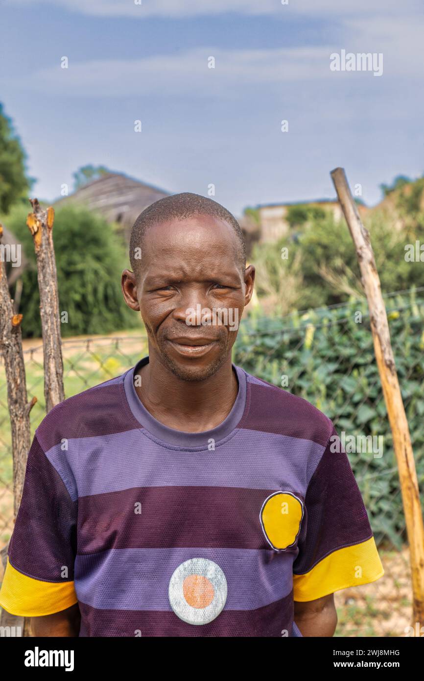 african man in the village, standing in the yard ,mud houses shacks ...