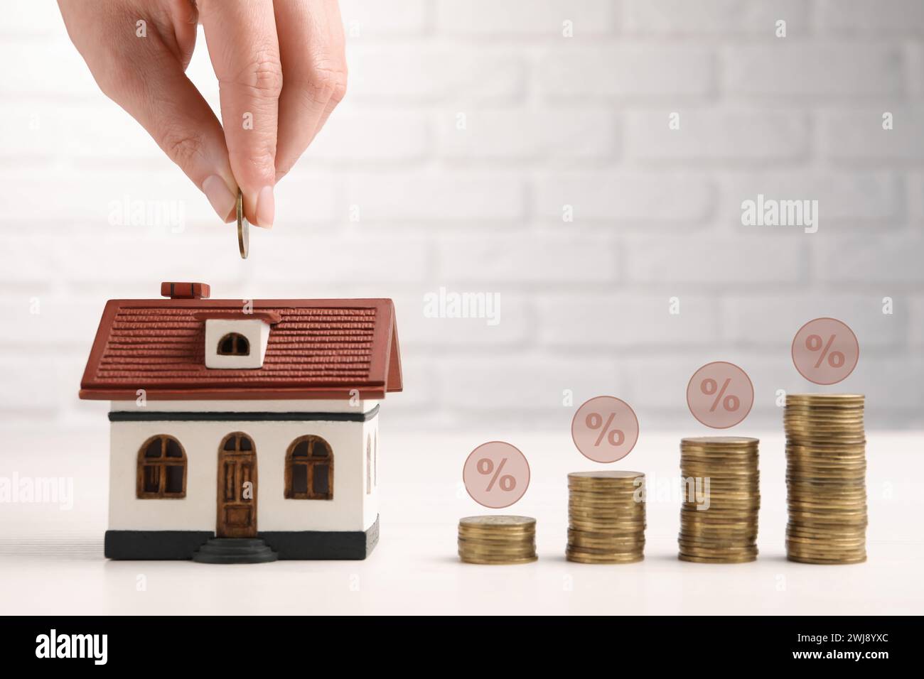 Mortgage rate. Woman putting coin into house shaped money box, closeup ...