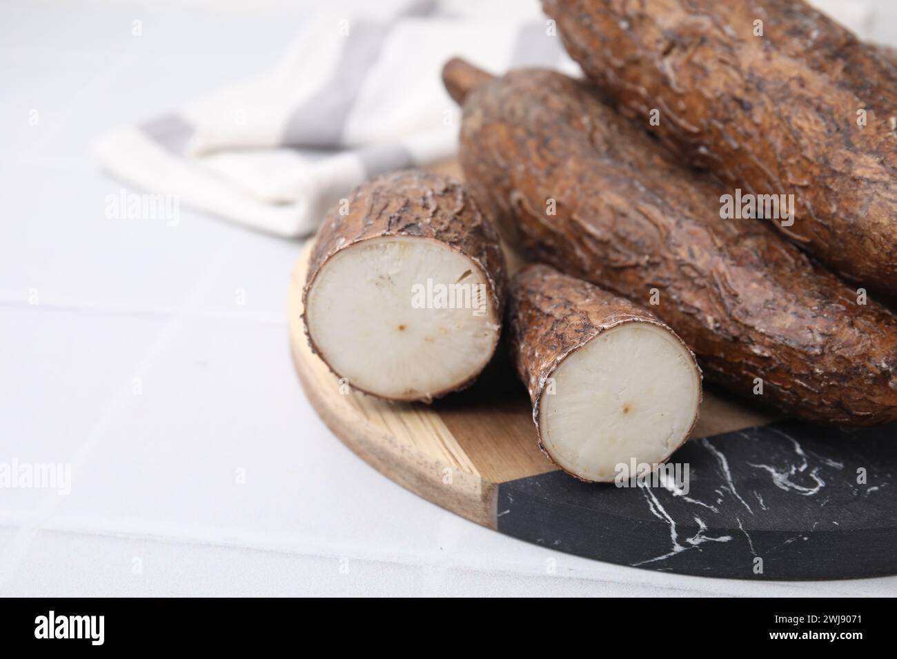 Whole and cut cassava roots on white tiled table, closeup. Space for ...