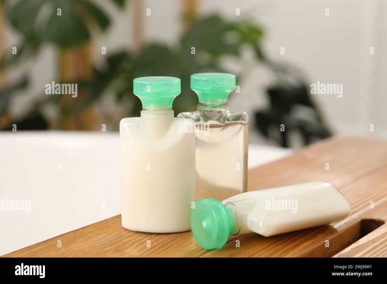 Wooden tray with mini bottles of cosmetic products on bath tub in ...
