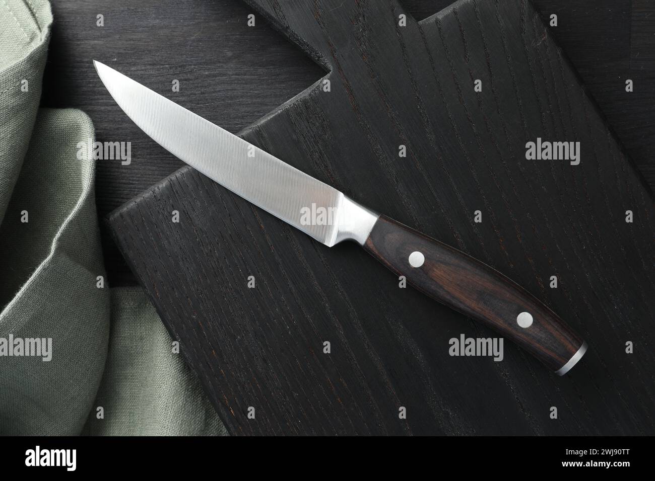 One sharp knife, cloth and board on black wooden table, top view Stock ...
