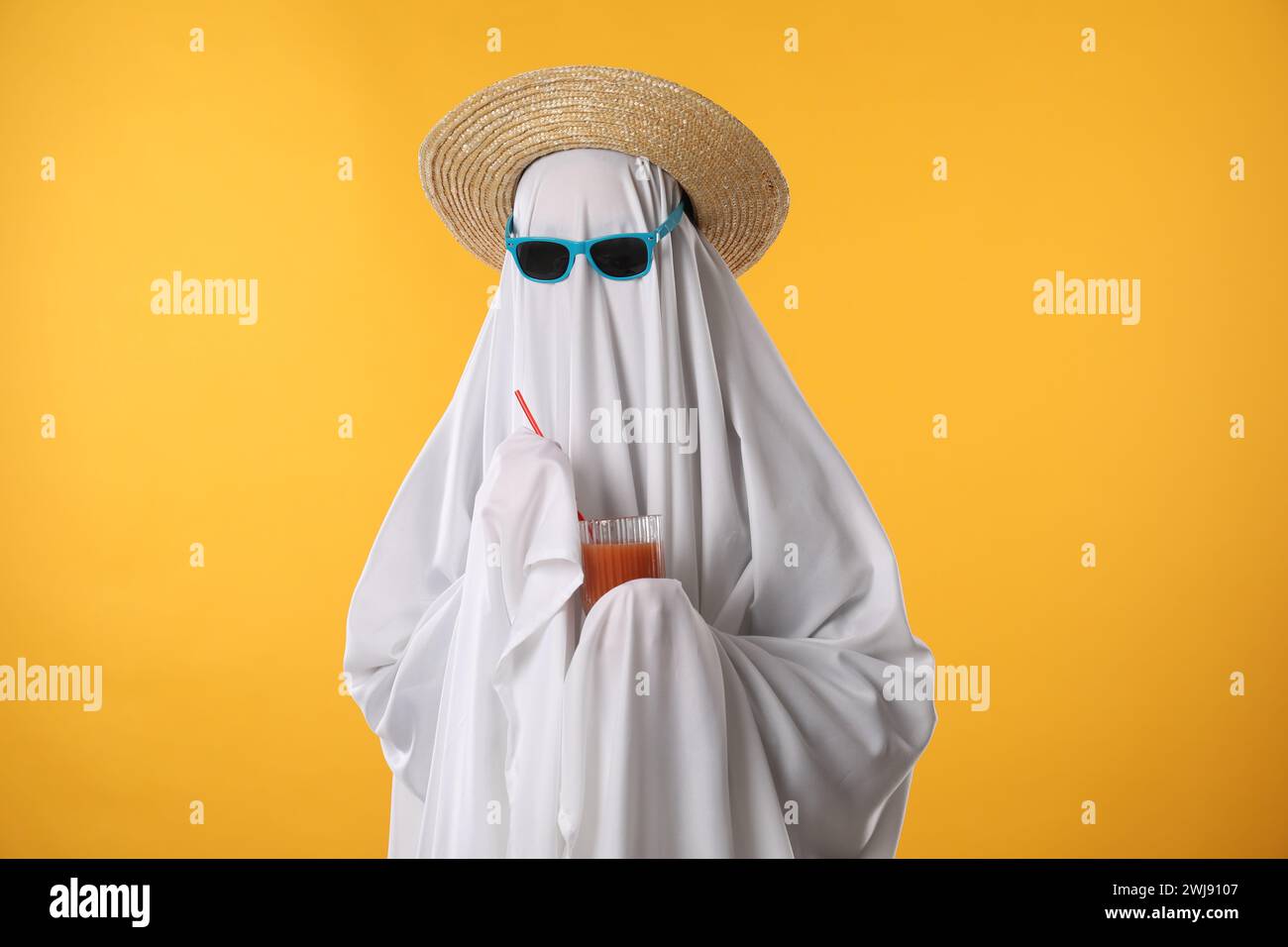Person in ghost costume, sunglasses and straw hat holding glass of ...