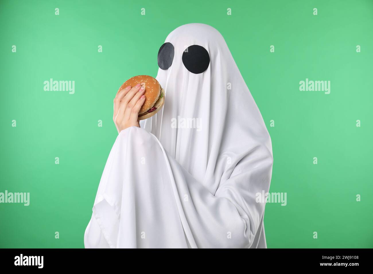 Creepy ghost. Person in white sheet with tasty hamburger on green ...