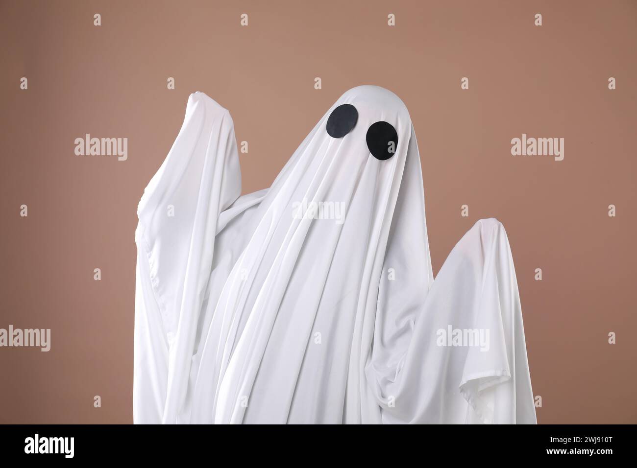 Creepy ghost. Person covered with white sheet on dark beige background ...
