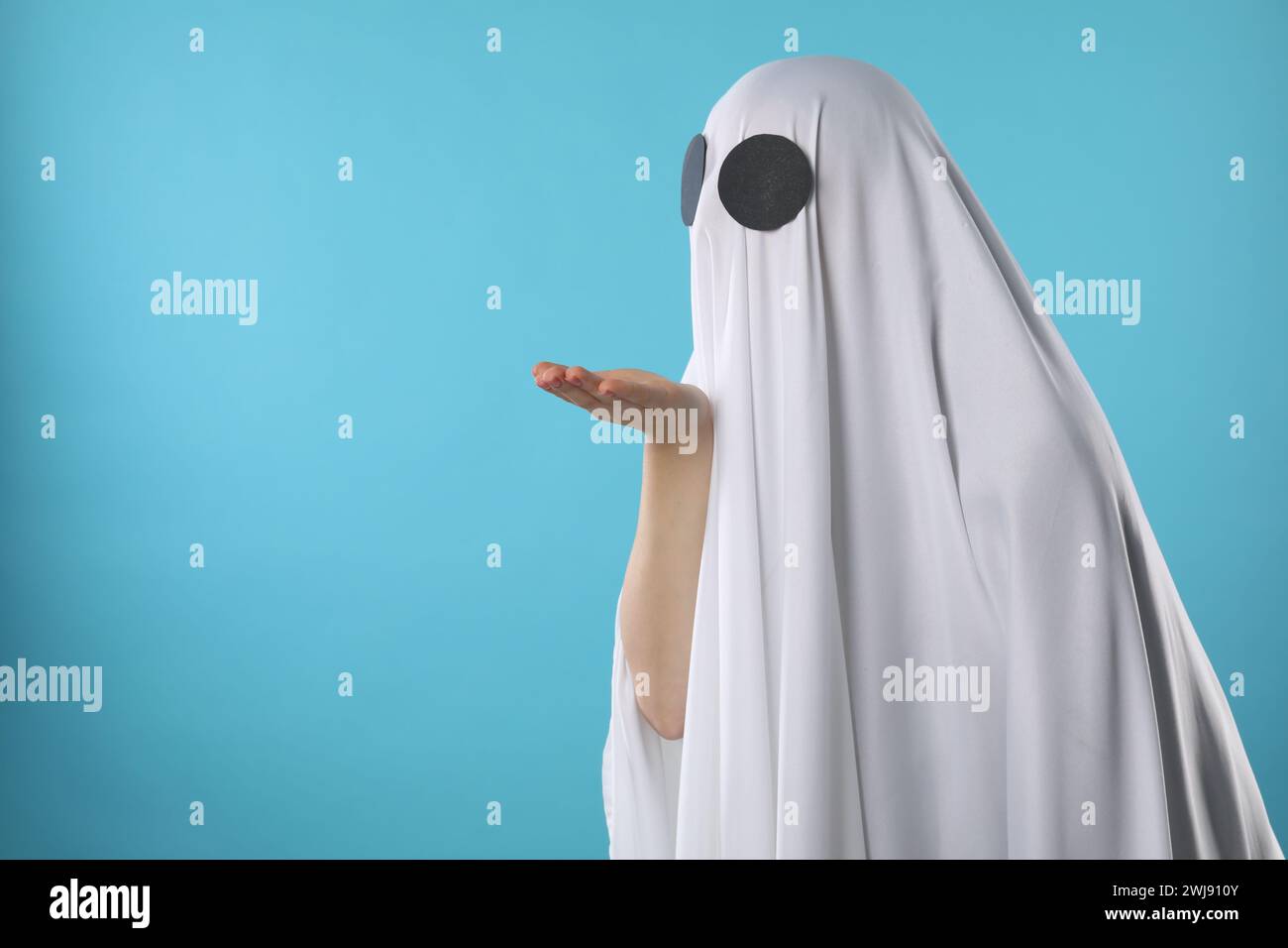 Creepy ghost. Woman covered with white sheet blowing kiss on light blue ...