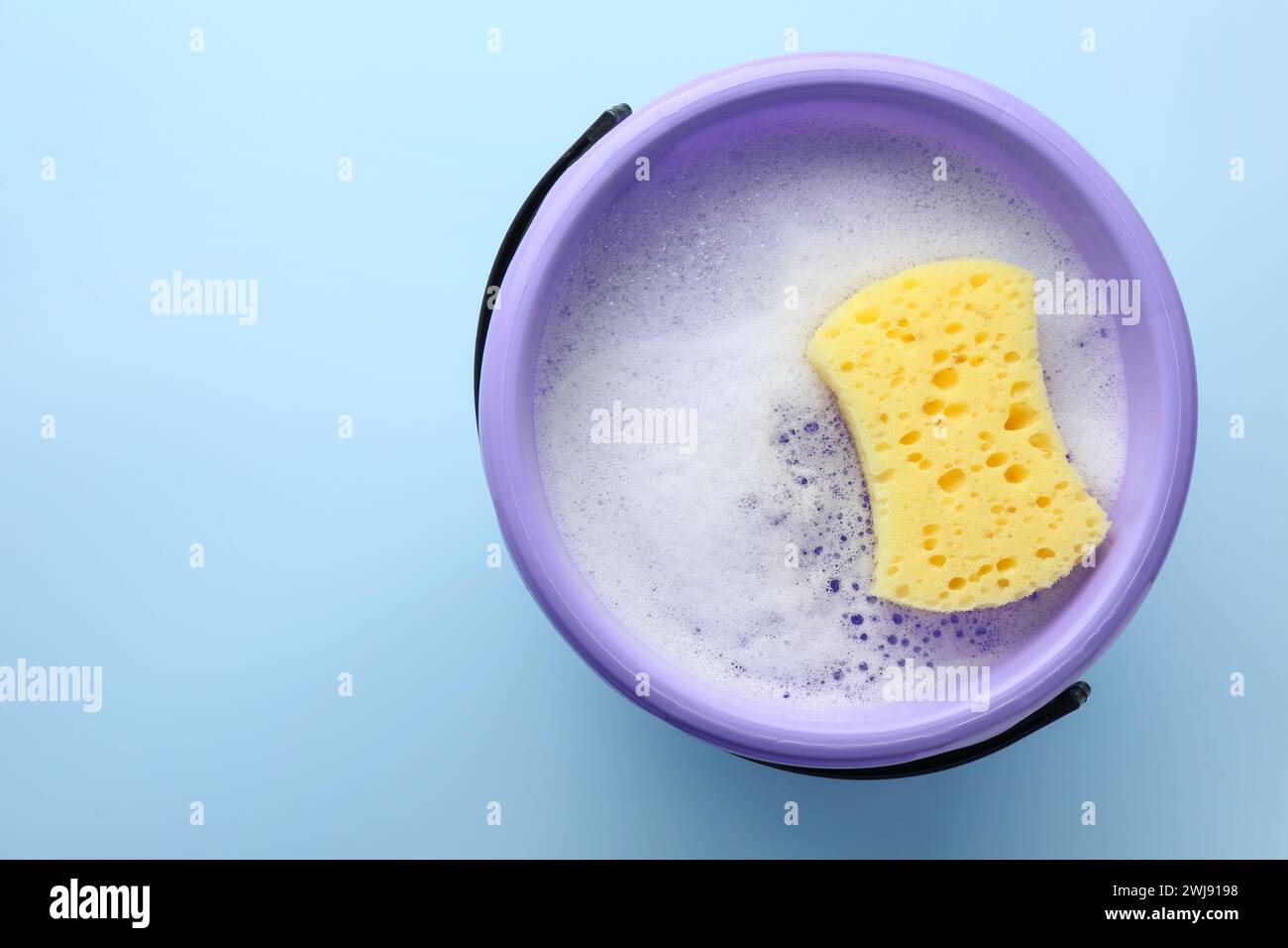 Bucket with foam and sponge on light blue background, top view. Space ...